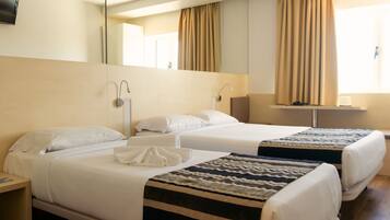 Quarto de hotel com duas camas, uma mesa de cabeceira, um espelho, janela com cortinas e televisão de tela plana.