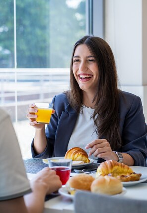 Uma pessoa sentada à mesa com um croissant e um copo de suco de laranja.