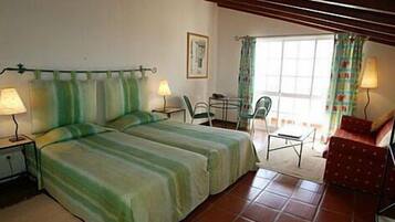 Quarto com cama, duas mesas de cabeceira, uma cadeira, uma mesinha e janela com cortinas.