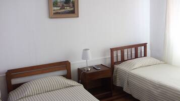 Quarto com duas camas de solteiro, uma mesa de cabeceira com abajur, um controle remoto e um quadro na parede.