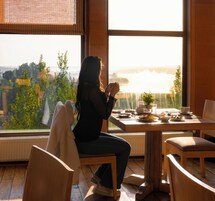 Uma pessoa sentada à mesa de madeira, com vista para a paisagem através de grandes janelas.
