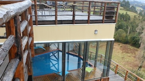 Um deck de madeira com uma banheira de hidromassagem, uma piscina com cobertura de vidro e um cercado de madeira.