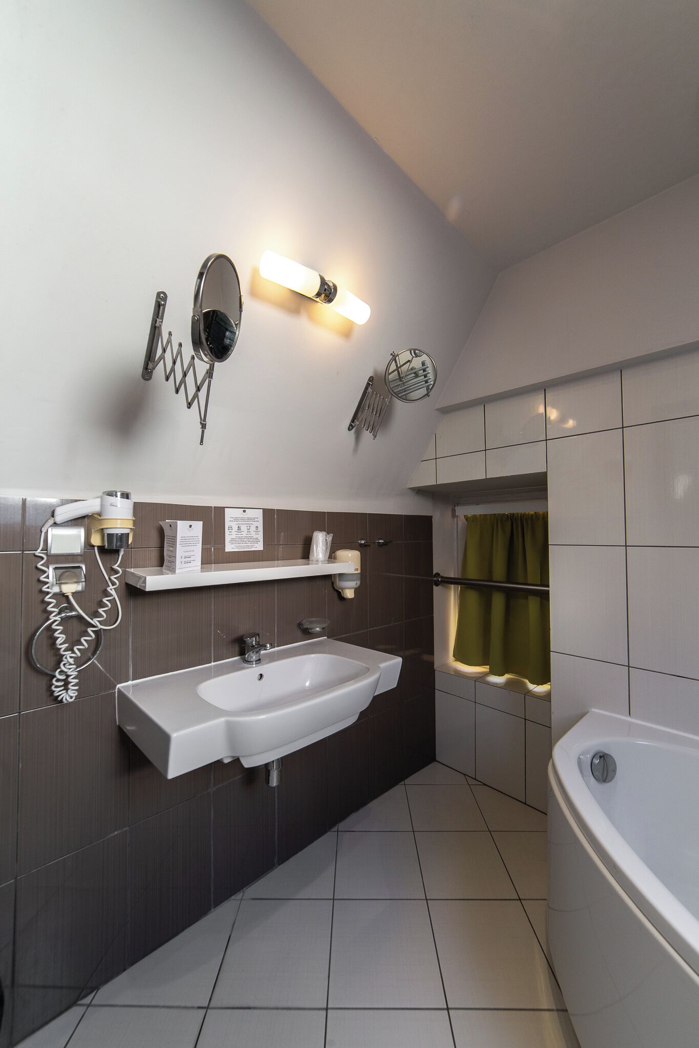 Casa de banho moderna com lavatório branco, uma banheira grande e um secador de cabelo fixado na parede.
