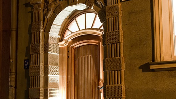 Uma entrada ornamentada com uma porta de madeira, uma placa verde acima e o número '36/39' na parede.