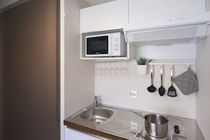 Uma cozinha compacta com micro-ondas embutido, pia com torneira moderna e uma pequena planta em vaso.