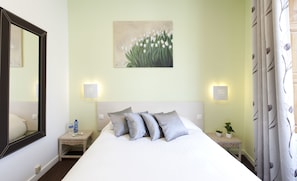 Quarto de hotel com uma cama grande, duas mesas de cabeceira, uma obra de arte na parede e um espelho.