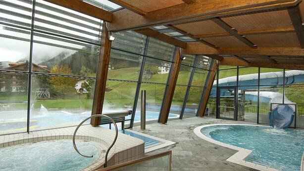 Piscina interior com vista para uma paisagem montanhosa através de grandes janelas.