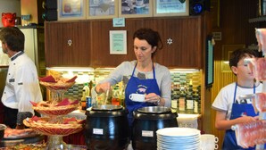 Disposição de buffet com diversos alimentos e um funcionário a servir.
