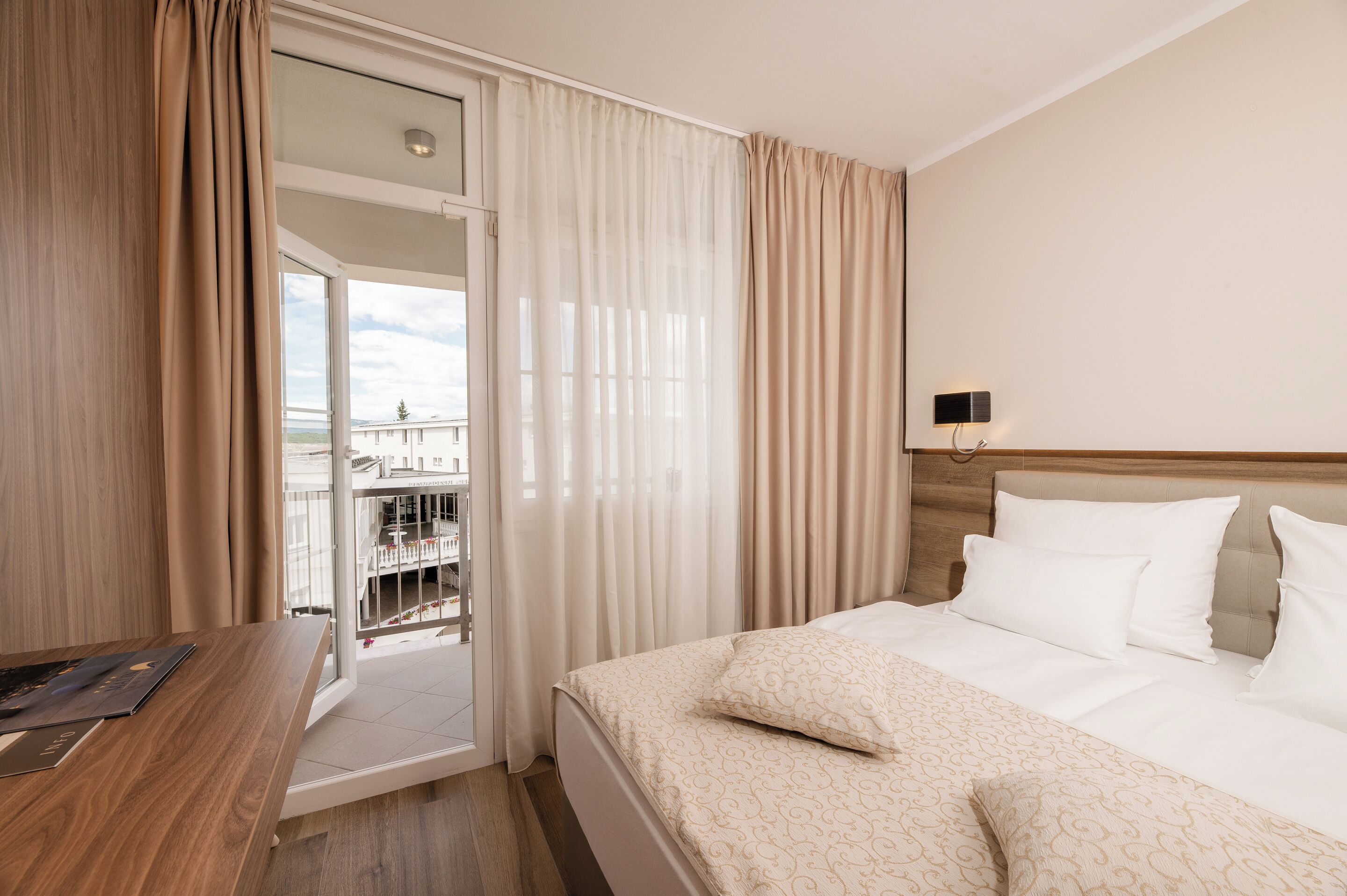 Quarto de hotel com cama, escrivaninha e vista para a varanda externa.