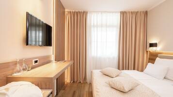 Quarto de hotel com cama, escrivaninha, televisão e janela com cortinas.