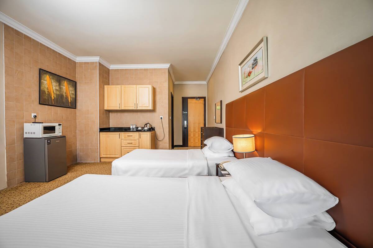 Quarto de hotel com duas camas, uma cozinha compacta, micro-ondas e mesa de cabeceira com abajur.