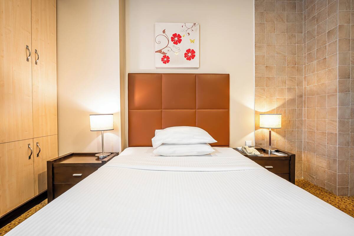 Quarto de hotel com uma cama grande, duas mesas de cabeceira com luminárias, uma cabeceira e uma obra de arte pendurada na parede.