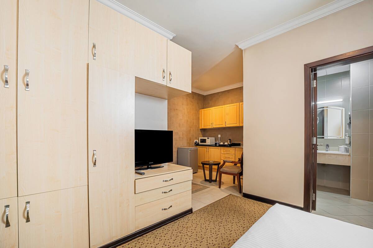 Quarto de hotel com cama, televisão, escrivaninha e cozinha compacta.