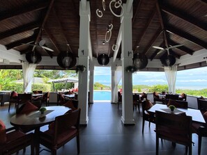 Restaurante com mesas e cadeiras, piscina ao fundo e vista para o oceano.