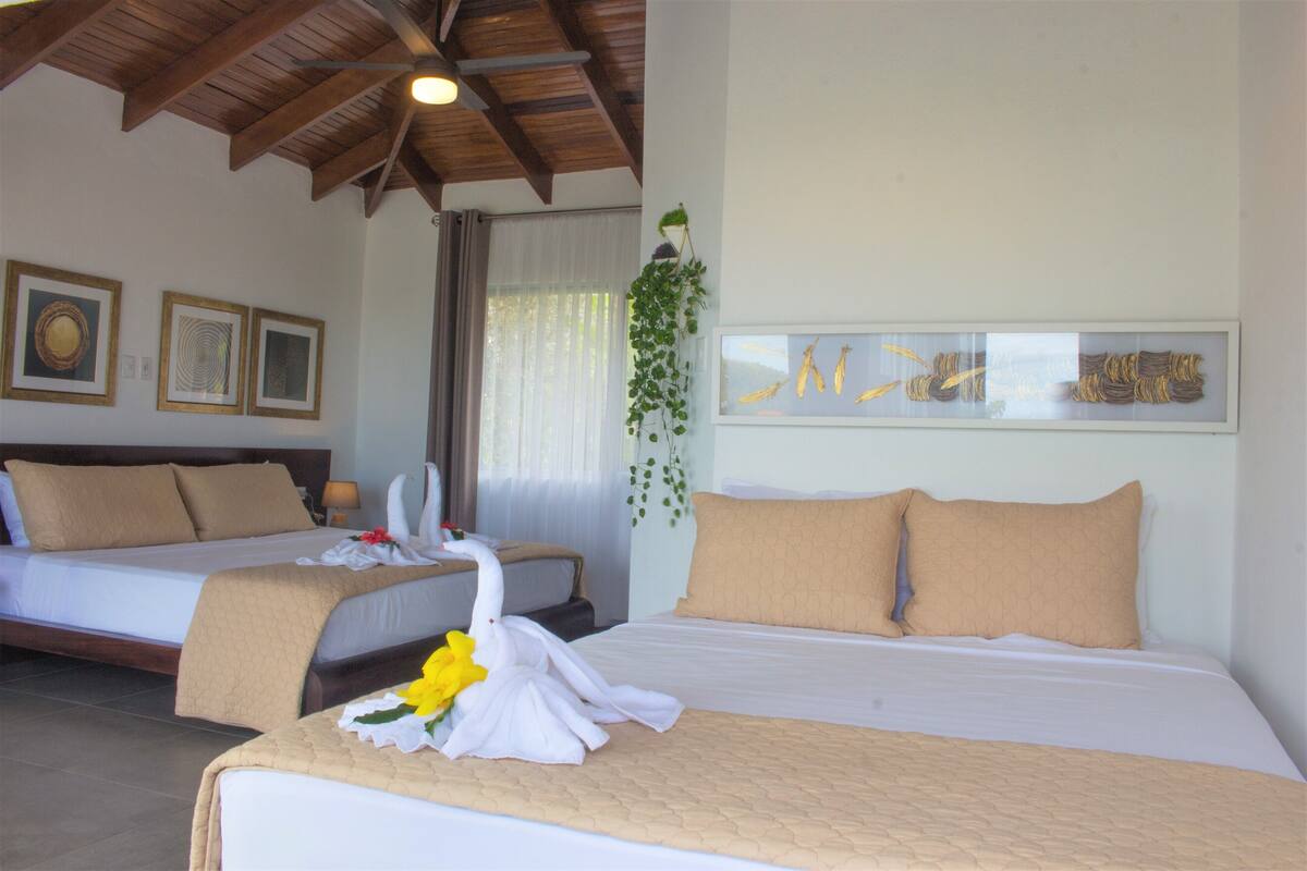 Quarto de hotel com duas camas, teto de madeira, obras de arte emolduradas na parede e uma planta.