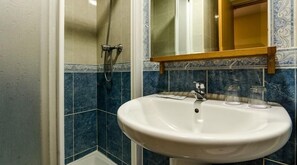 Casa de banho com lavatório branco, chuveiro manual e espelho sobre o lavatório.