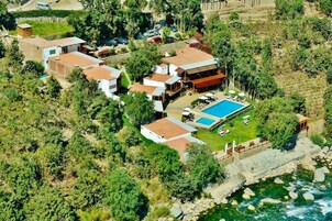 Vista aérea de um resort costeiro com várias villas, piscina e uma orla rochosa.