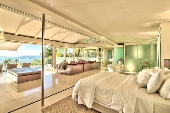 Quarto moderno com uma cama grande, área de estar e vista para o oceano.