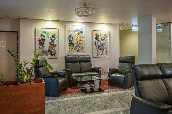 Um hall com poltronas de couro, uma mesa de centro de vidro e arte abstrata nas paredes.