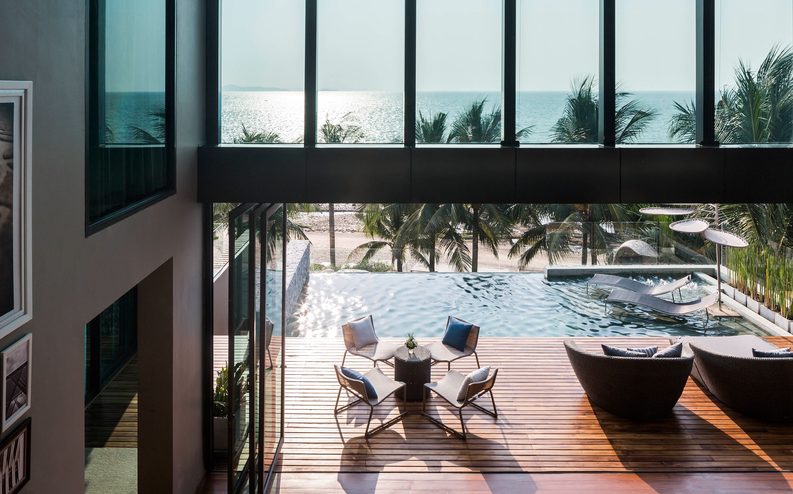 Um deck moderno ao ar livre com vista para o mar, piscina e espreguiçadeiras.