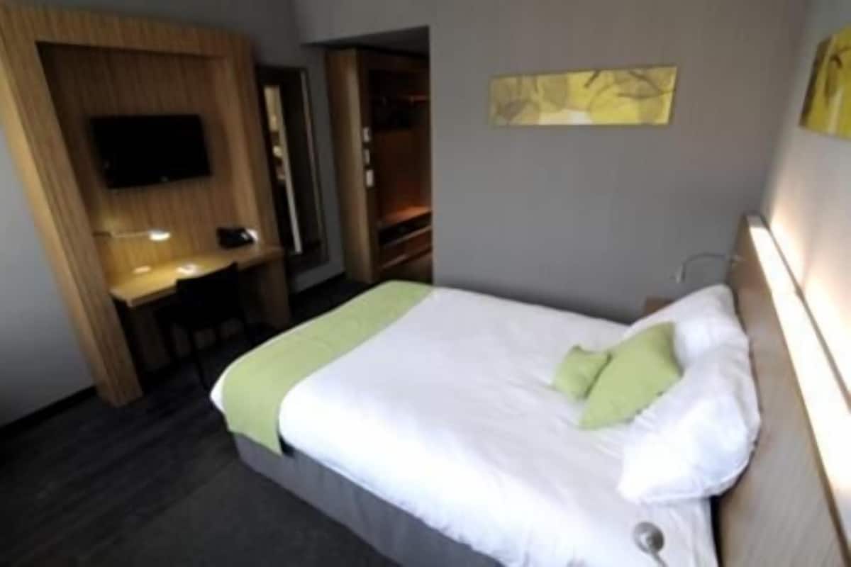 Quarto de hotel com cama, escrivaninha e televisão.
