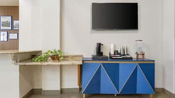 Uma área de recepção de hotel com uma televisão de tela plana na parede, uma máquina de café e uma planta no balcão.