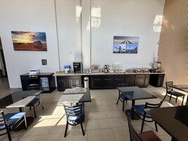 Cozinha moderna com espaço para café, área de jantar com mesas e cadeiras, e obras de arte nas paredes.