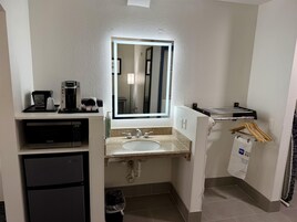 Casa de banho de hotel compacta com lavatório, espelho, máquina de café e frigorífico pequeno.