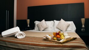 Quarto de hotel com cama bem arrumada, bandeja de café da manhã com frutas e doces, e toalha dobrada na cama.