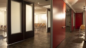 Sala de conferências moderna com divisória de vidro, porta vermelha e área de estar com cadeiras.