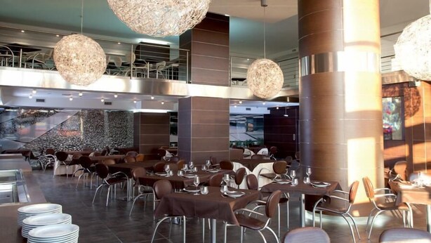 Restaurante moderno com mesas e cadeiras redondas, grandes luminárias esféricas pendentes e uma escadaria que dá acesso a um andar superior.