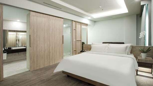 Quarto de hotel moderno com uma cama grande, um closet espaçoso, banheiro com espelho e uma planta em vaso.