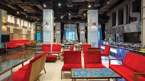 Um restaurante moderno com assentos estofados em vermelho, um bar e vista para a cidade através de grandes janelas.