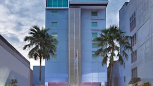 Hotel moderno com fachada vertical de vidro, palmeiras e céu claro.