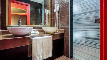 Uma casa de banho moderna com duas pias grandes, um espelho com moldura vermelha e cabine de duche em vidro.