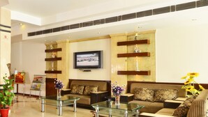 Um hall amplo com um conjunto de sofás moderno, uma TV de tela plana na parede e uma mesa de centro de vidro.