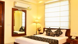 Quarto de hotel com uma cama grande, mesa de cabeceira com abajur, espelho, ar condicionado e janela com cortinas.