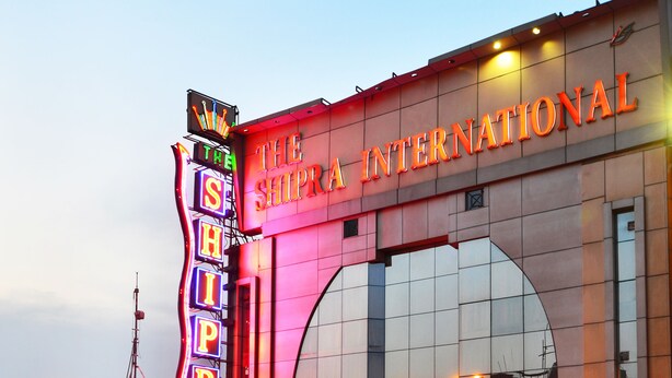 Hotel Shipra International, com placa visível e fachada espelhada em vidro.