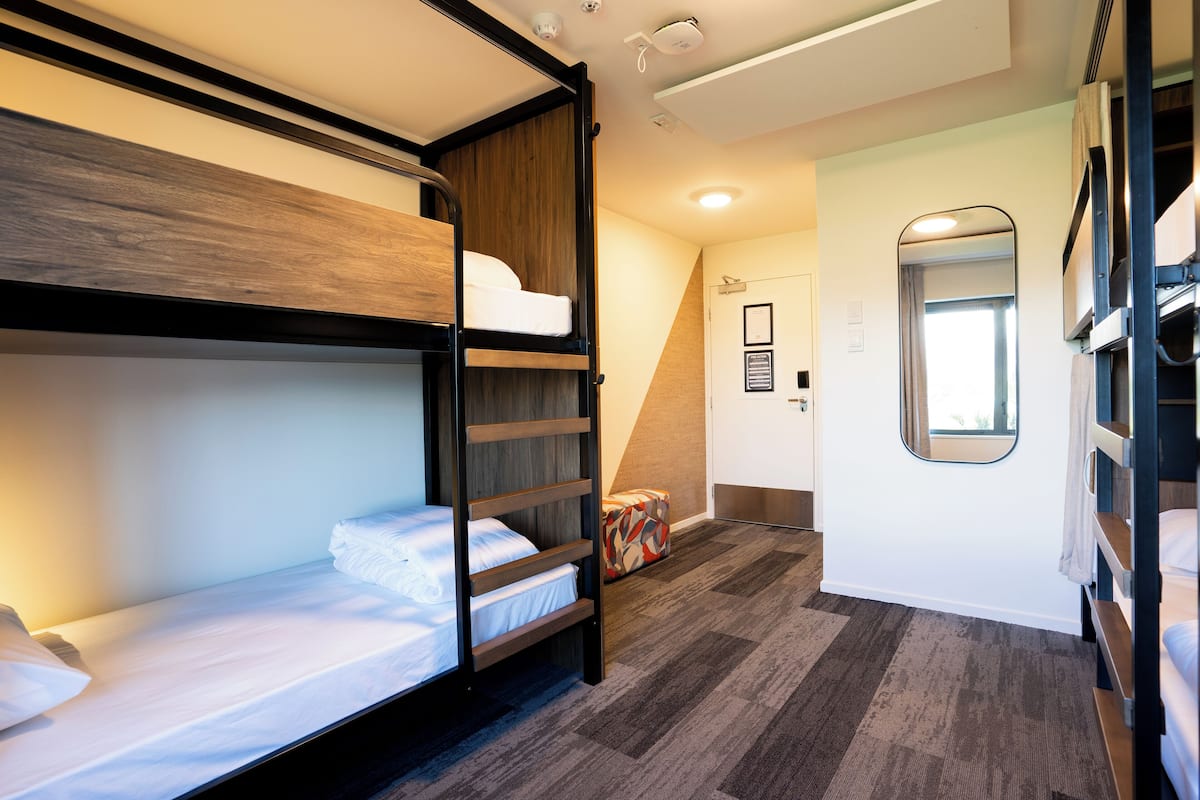 Quarto com beliche, cabeceira de madeira, um banquinho e um espelho na parede.