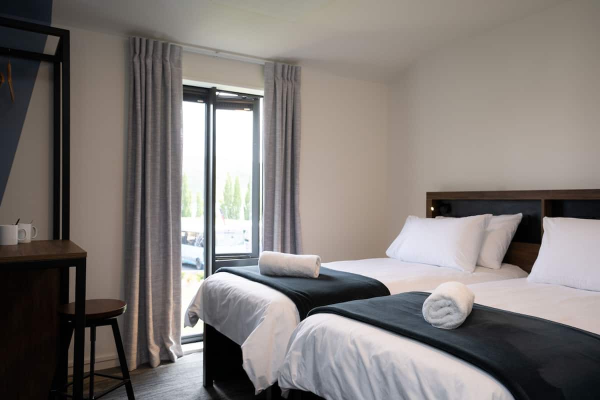Quarto de hotel com duas camas, uma escrivaninha e uma janela com cortinas.