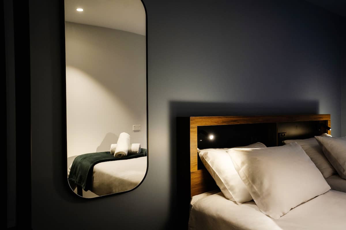 Quarto de hotel moderno com um espelho grande, uma cama bem arrumada e cabeceira de madeira.
