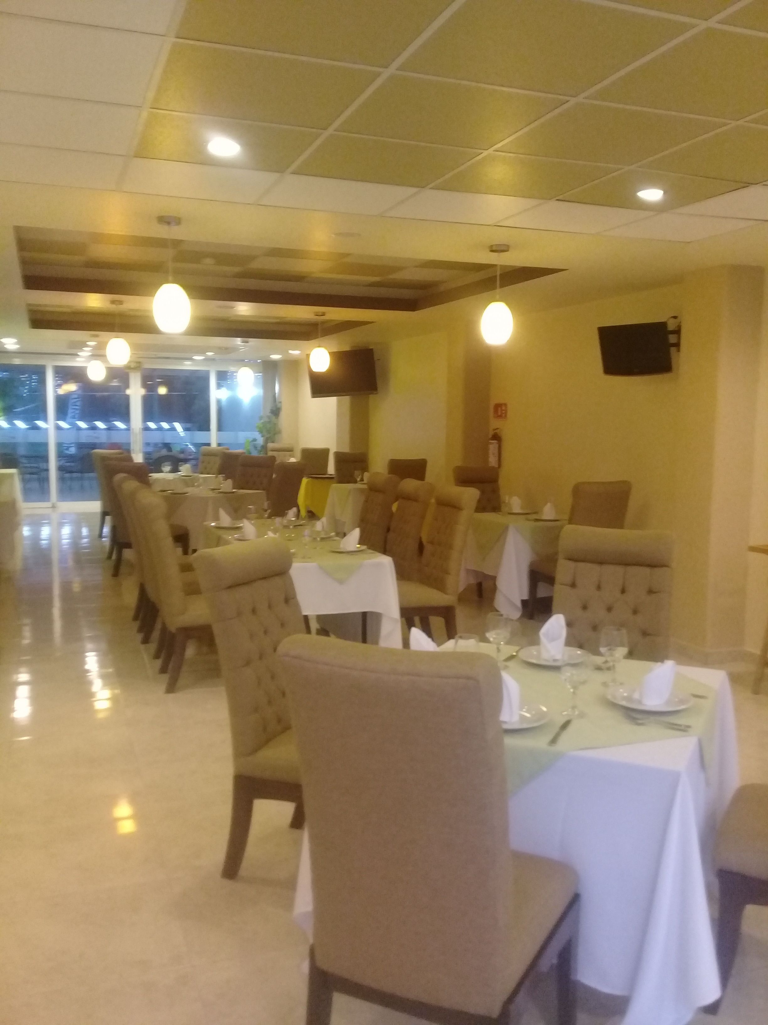 Um restaurante com várias mesas postas para refeições, cadeiras e uma televisão na parede.