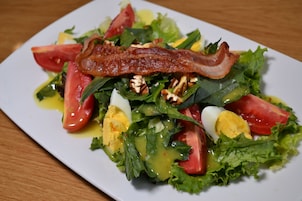 Salada com bacon, ovos e tomates em um prato branco.