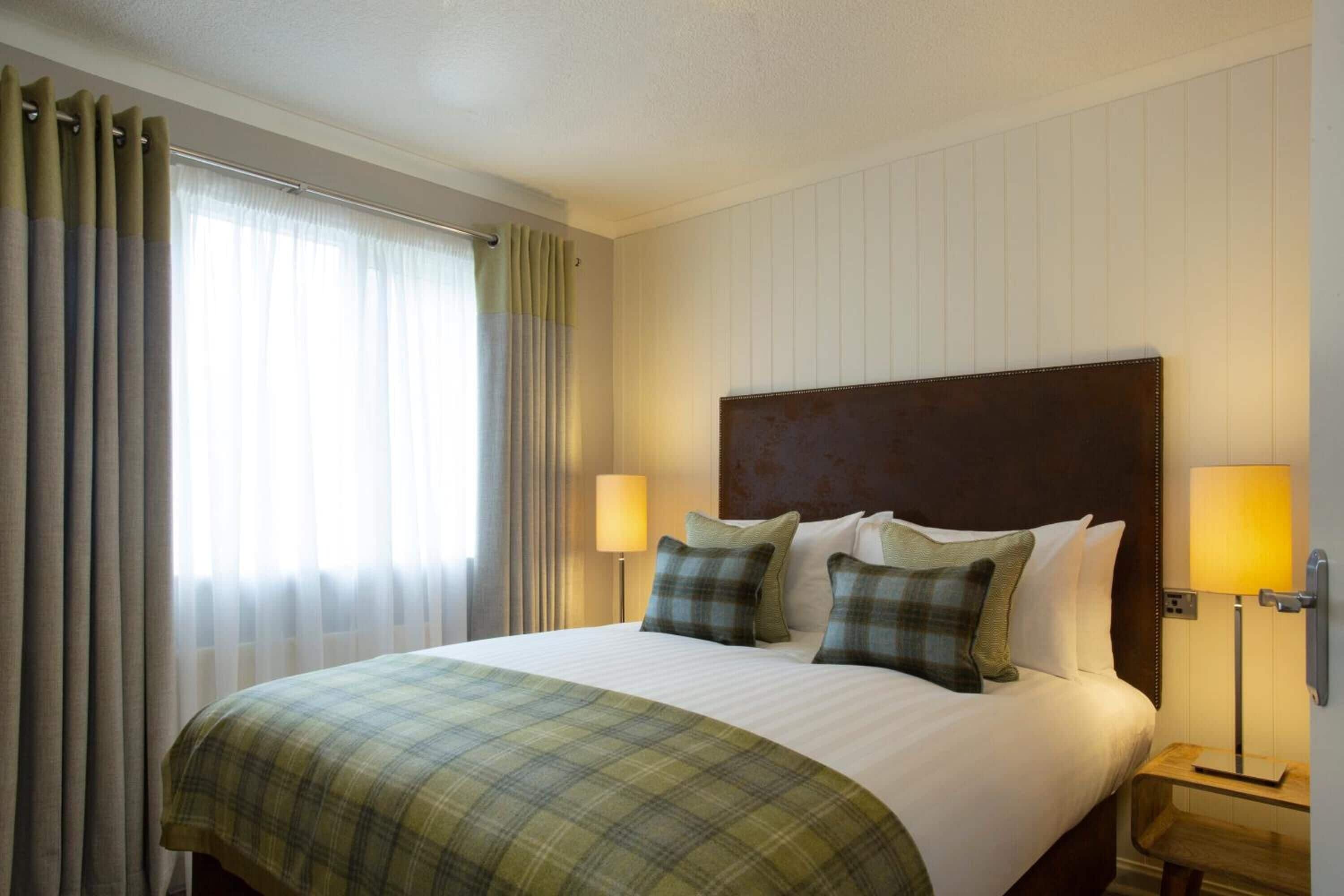 Quarto de hotel com uma cama grande, duas luminárias de cabeceira e uma janela com cortinas.
