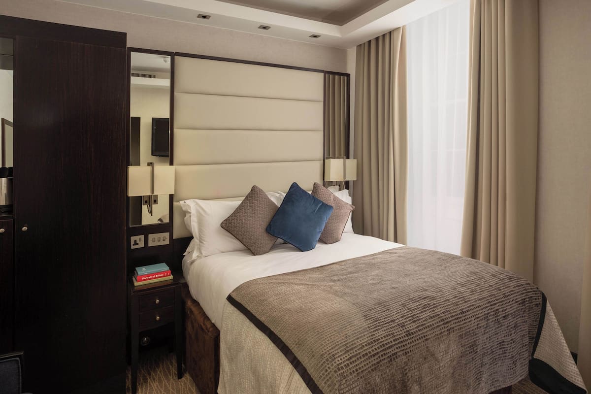 Quarto de hotel com uma cama grande, mesa de cabeceira com abajur, guarda-roupa e espelho.