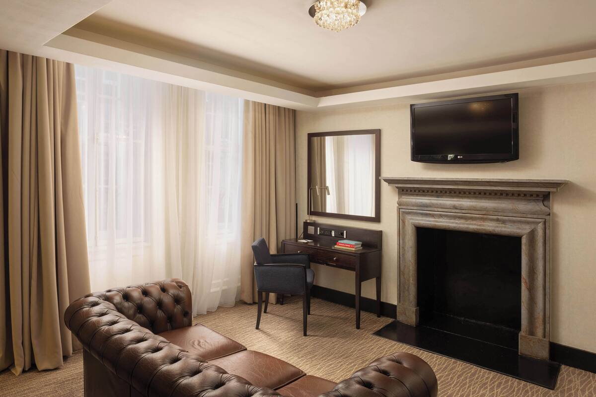 Quarto de hotel com sofá de couro, escrivaninha, televisão e lareira.