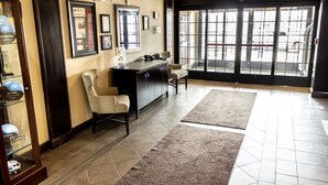 Um hall de entrada com balcão de recepção, quadros nas paredes e uma grande porta de vidro que dá para o exterior.