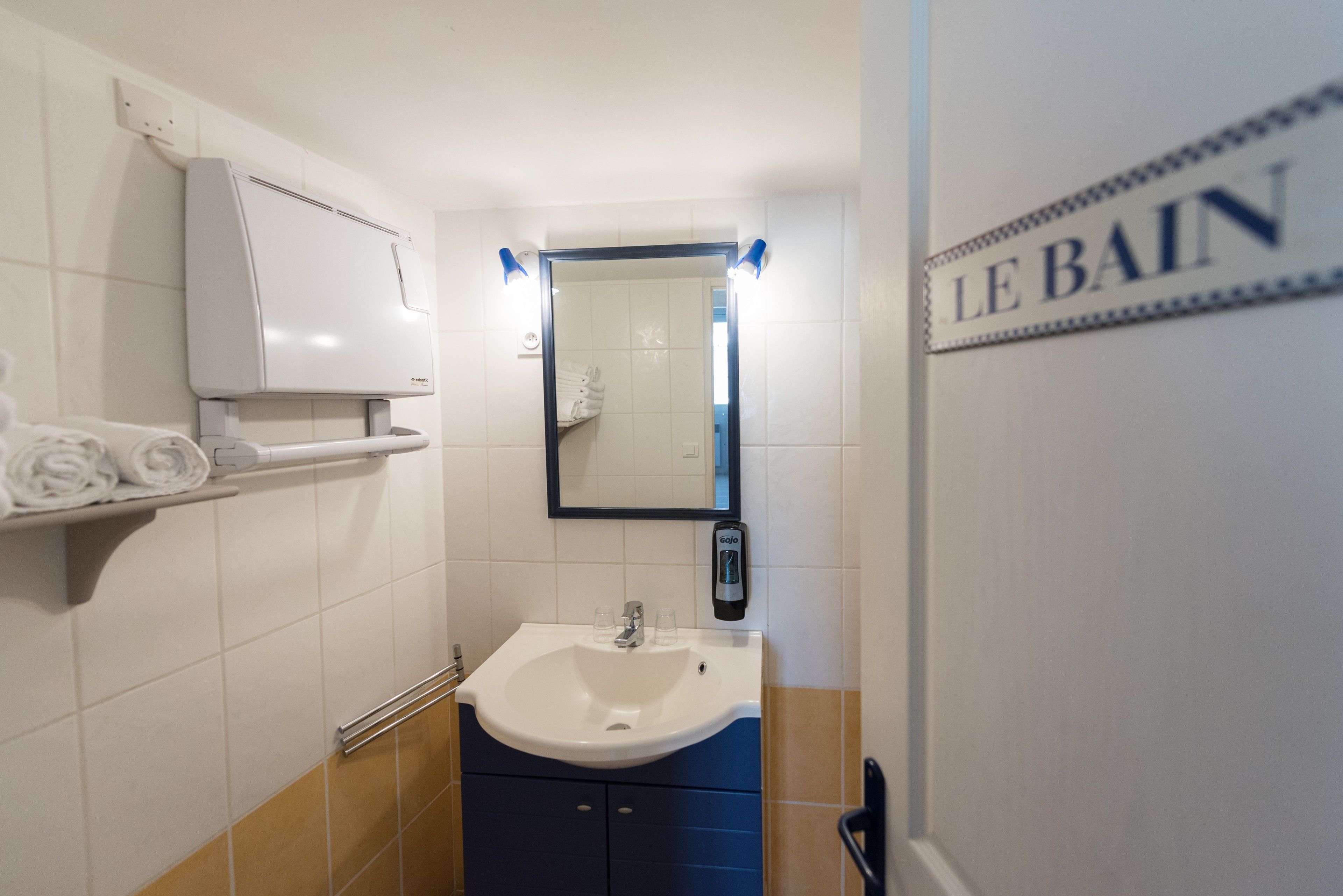 Uma casa de banho com uma pia branca, um espelho e um porta-toalhas.
