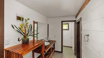 Casa de banho com toucador de madeira, lavatório, espelho e uma planta em vaso.
