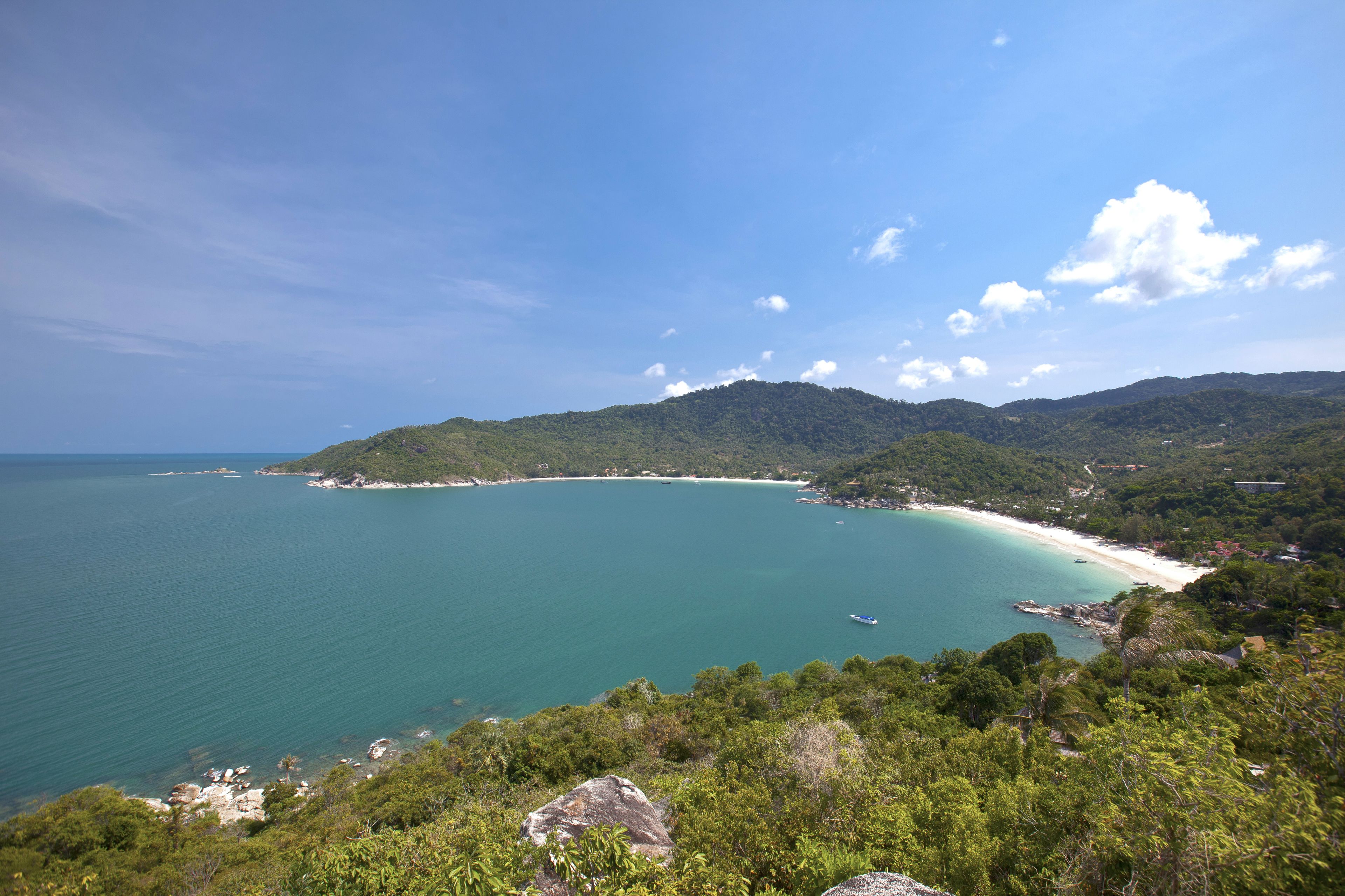 Paisagem costeira com praia, mar azul cristalino e colinas verdes exuberantes.